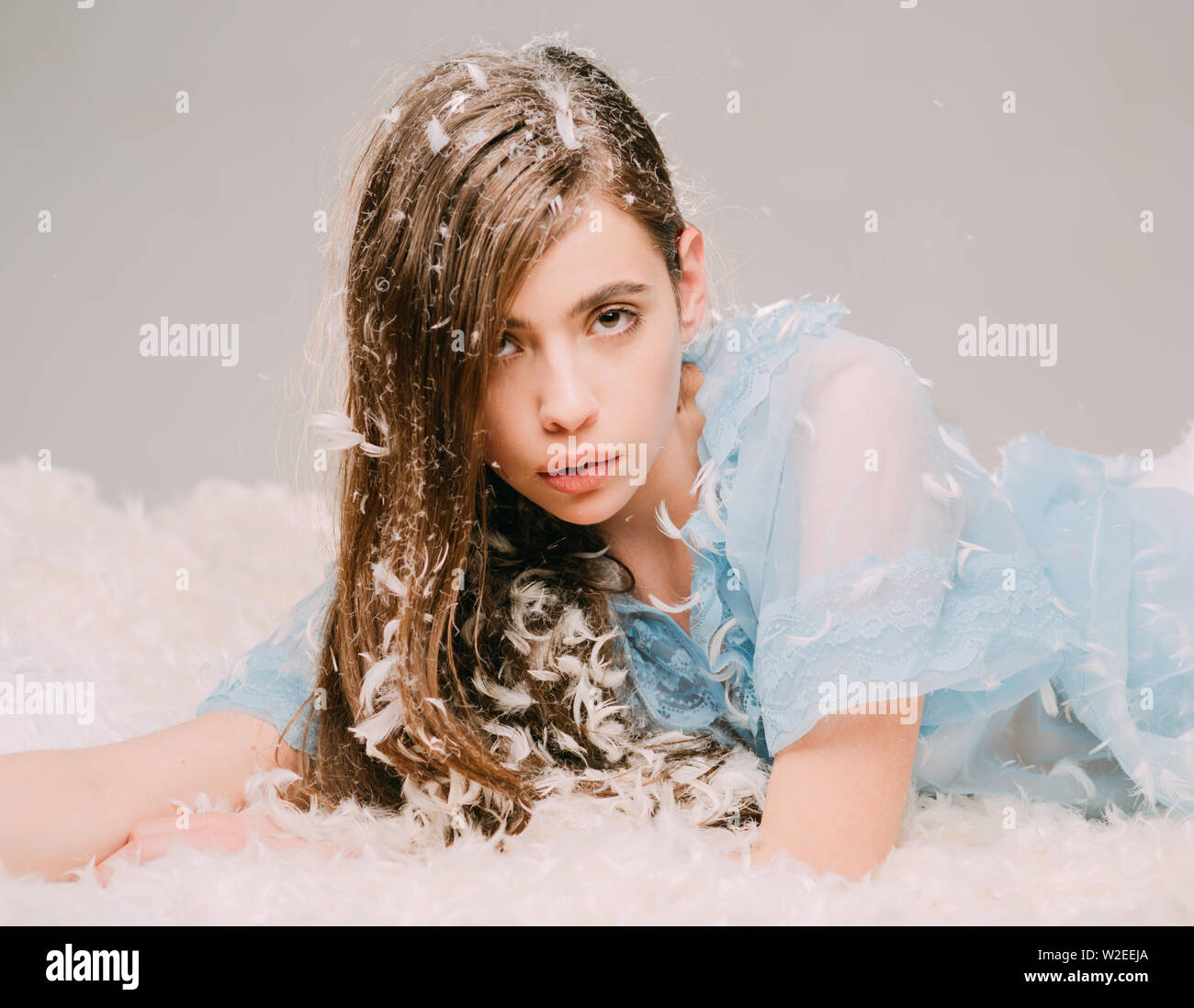 Beautiful girl with fluff in her hair lying on downy bed full of ...