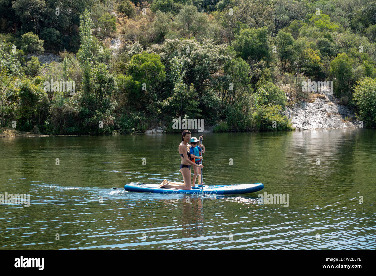 Young mother teaching a little boy how to use a Paddle Board on a lake ...