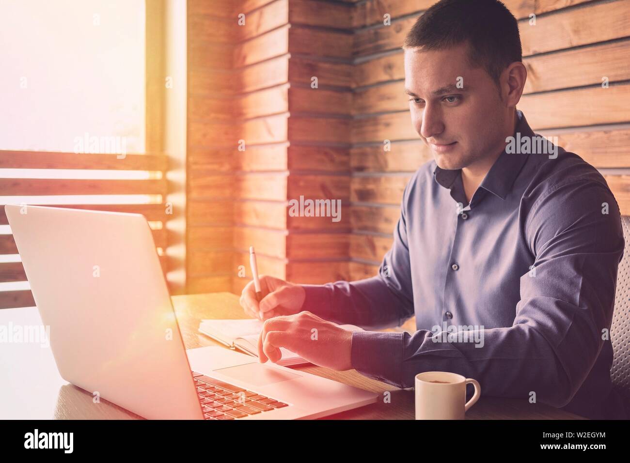 Businessman making notes while using a laptop computer at a desk in an ...