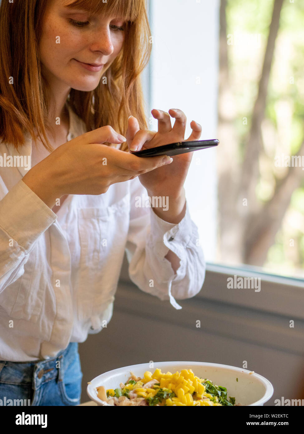 Caucasian girl in a modern kitchen, consult her cell phone to know the ...