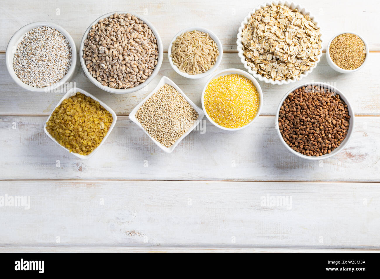 Selection of whole grains in white bowls - rice, oats, buckwheat ...