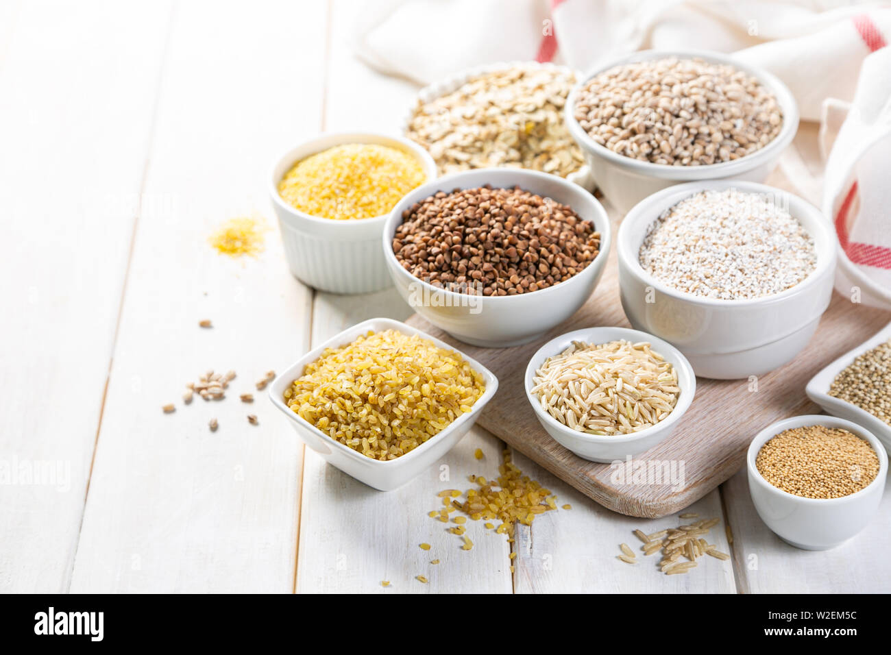 Selection of whole grains in white bowls - rice, oats, buckwheat ...