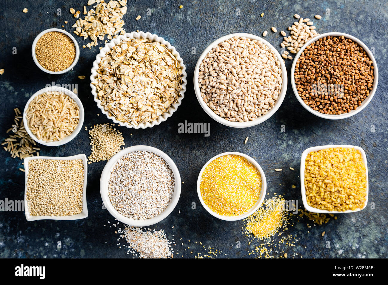 Selection of whole grains in white bowls - rice, oats, buckwheat ...