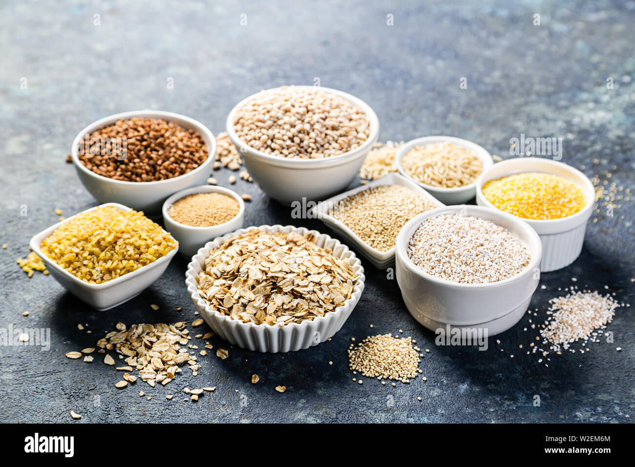 Selection of whole grains in white bowls - rice, oats, buckwheat ...