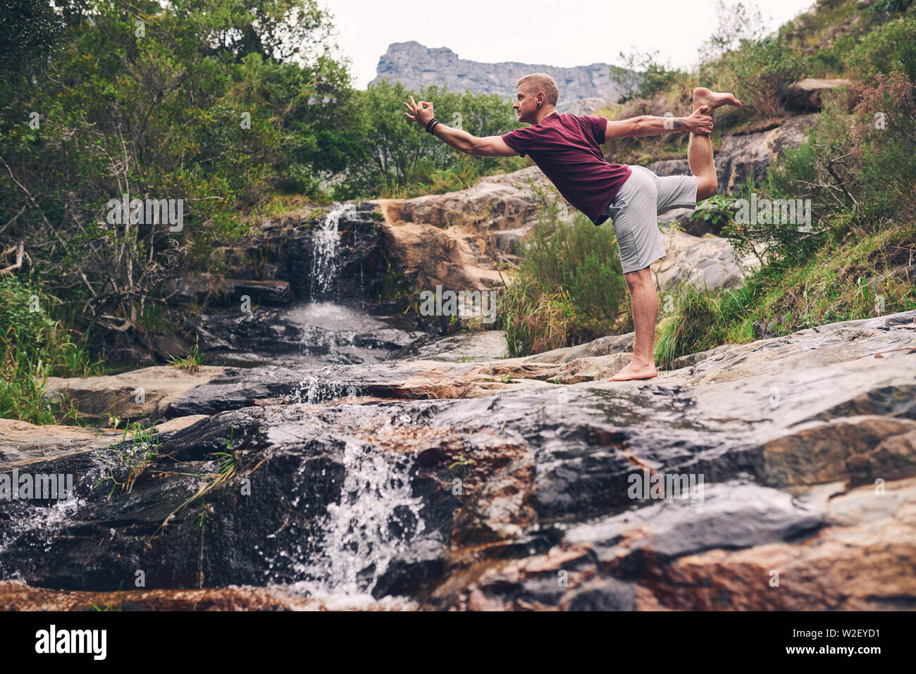 Fit man doing the dancer pose by a waterfall Stock Photo - Alamy