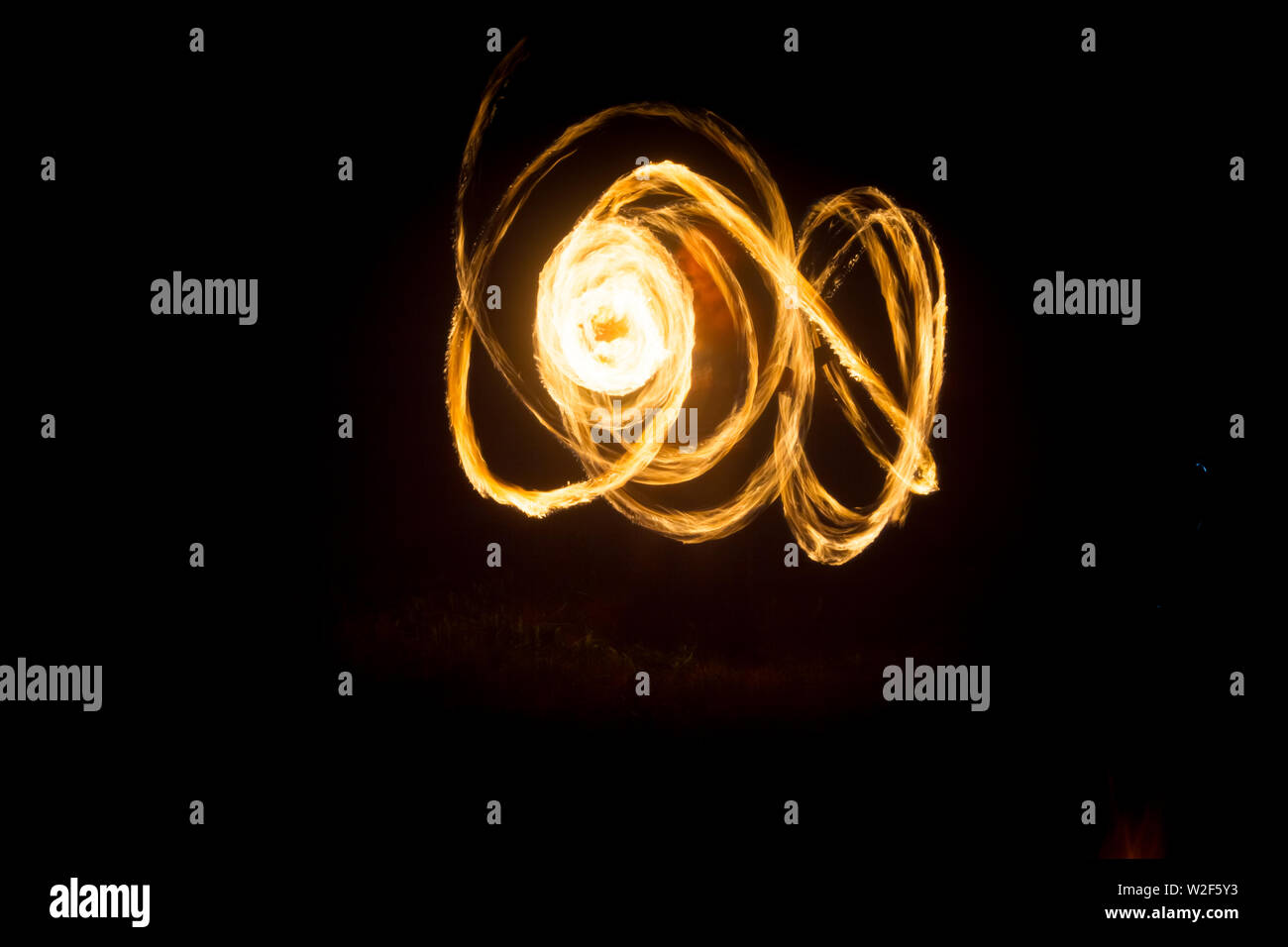 An artist shows a fire show at night spinning torches, circles of fire ...