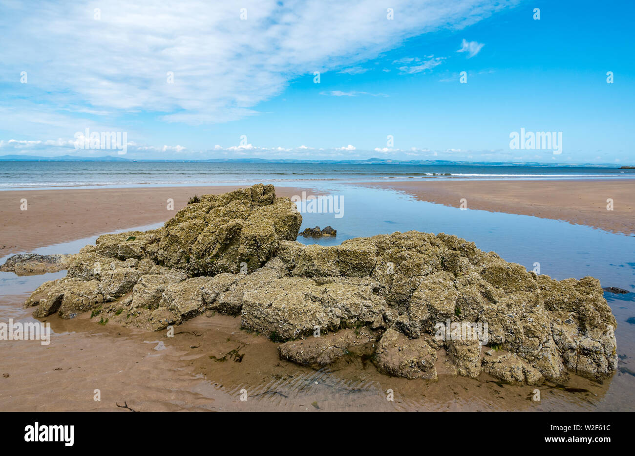 Gullane beach on sunny Summer day with rock covered in barnacles, Forth ...
