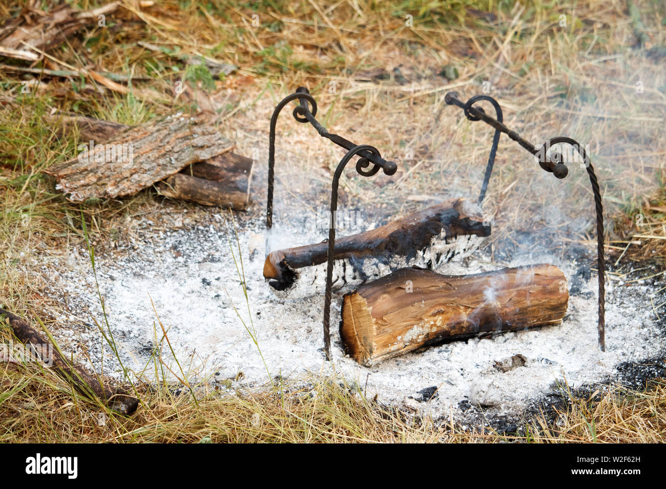 An extinguished fire with burnt wood near the metal racks for cooking ...