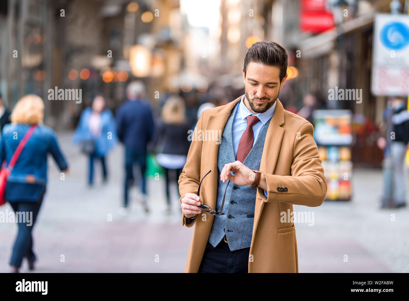 A handsome elegant man walking on the streets and checking the time on ...