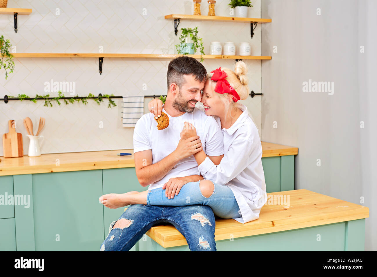 Beautiful affectionate couple sitting on the kitchen table are hugging ...