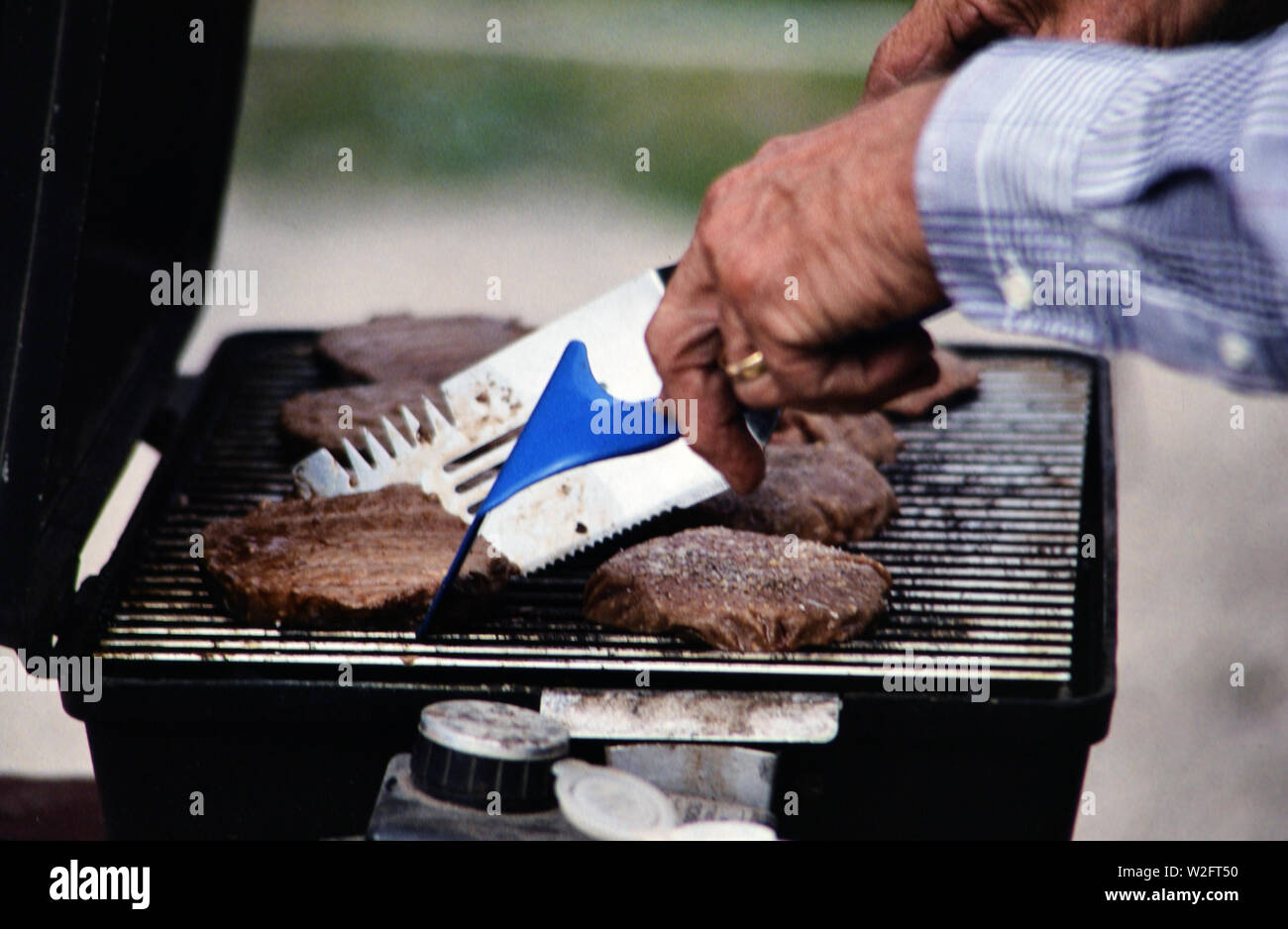 Man girlling steaks on an outdoor grill prepares to flip one steak over ...