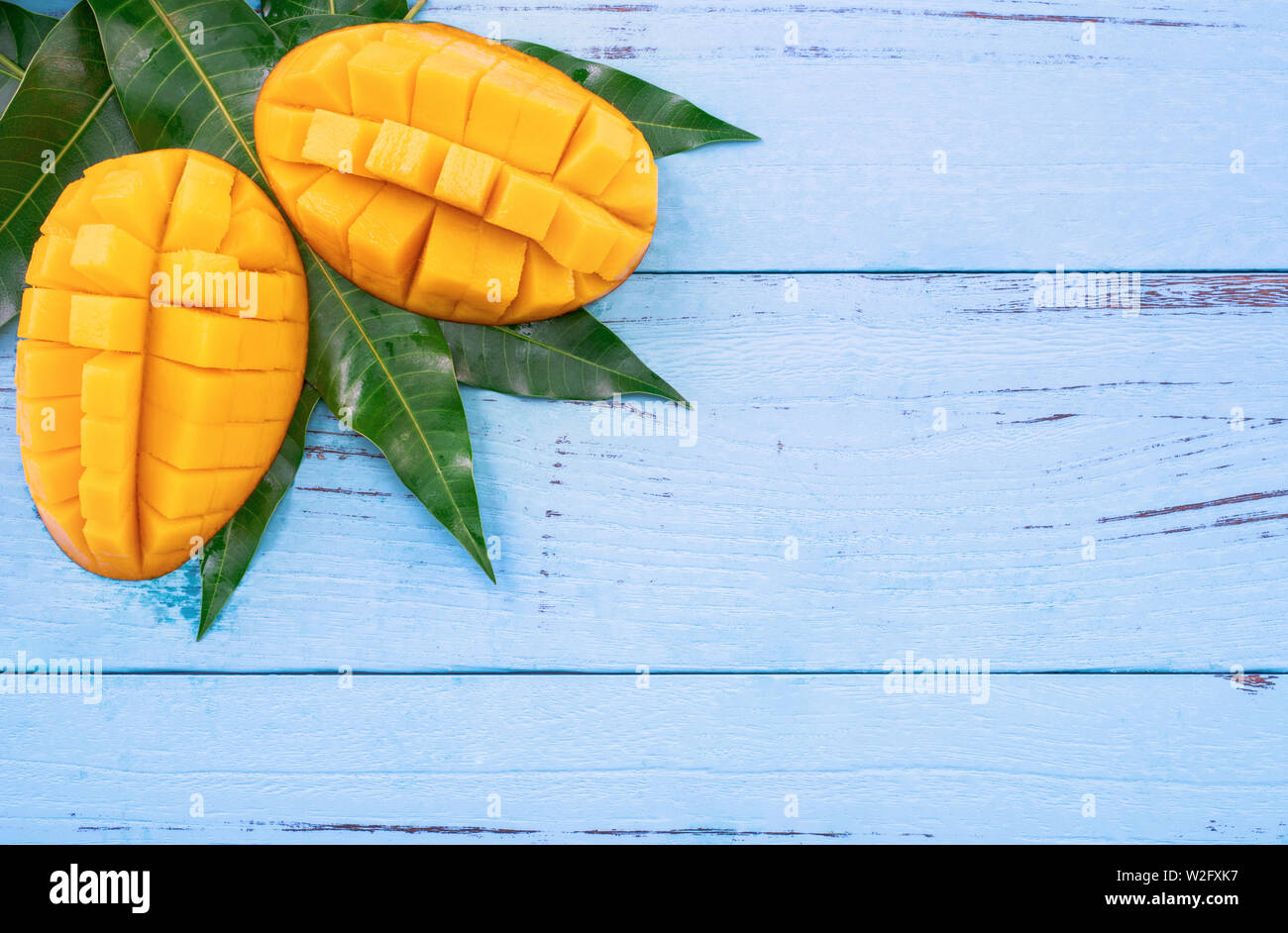 Fresh chopped mango with green leaves on bright blue color timber ...