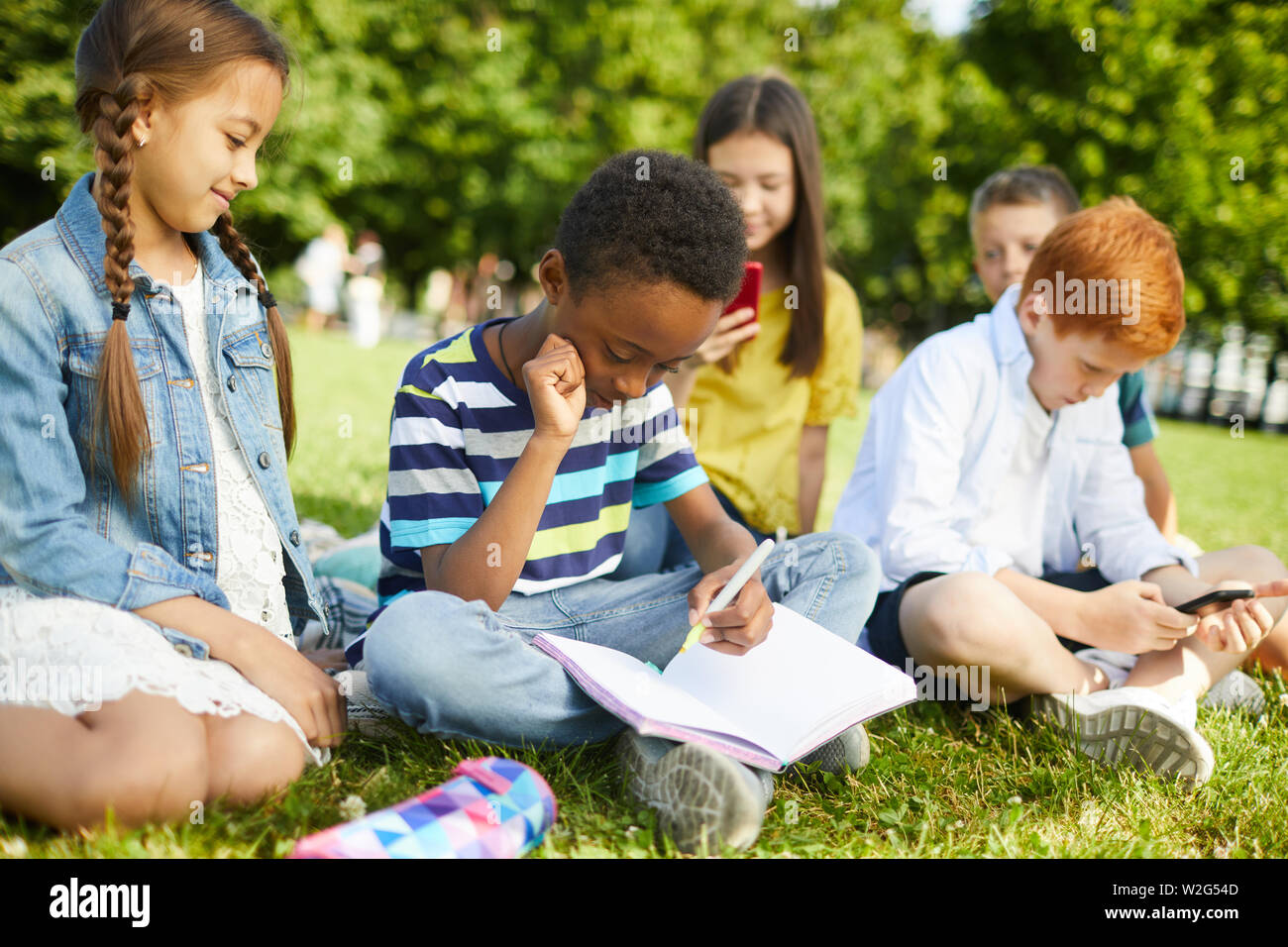 Two teenage friends doing homework outside sitting on grass while their ...