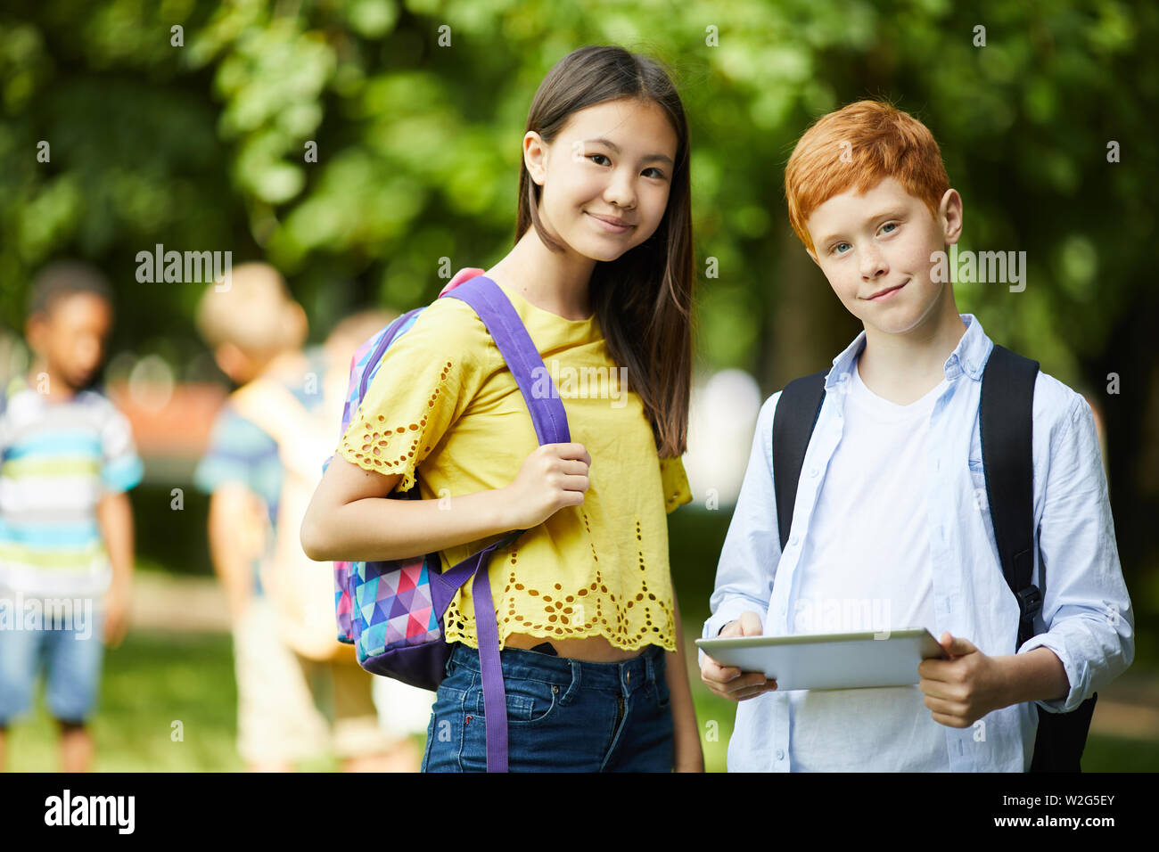 Two smiling schoolchildren standing outside in front of school and ...