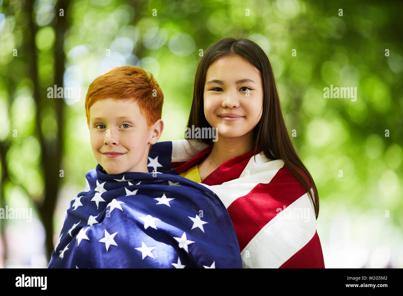 Portrait of smiling cute little Americans huddled in national flag ...