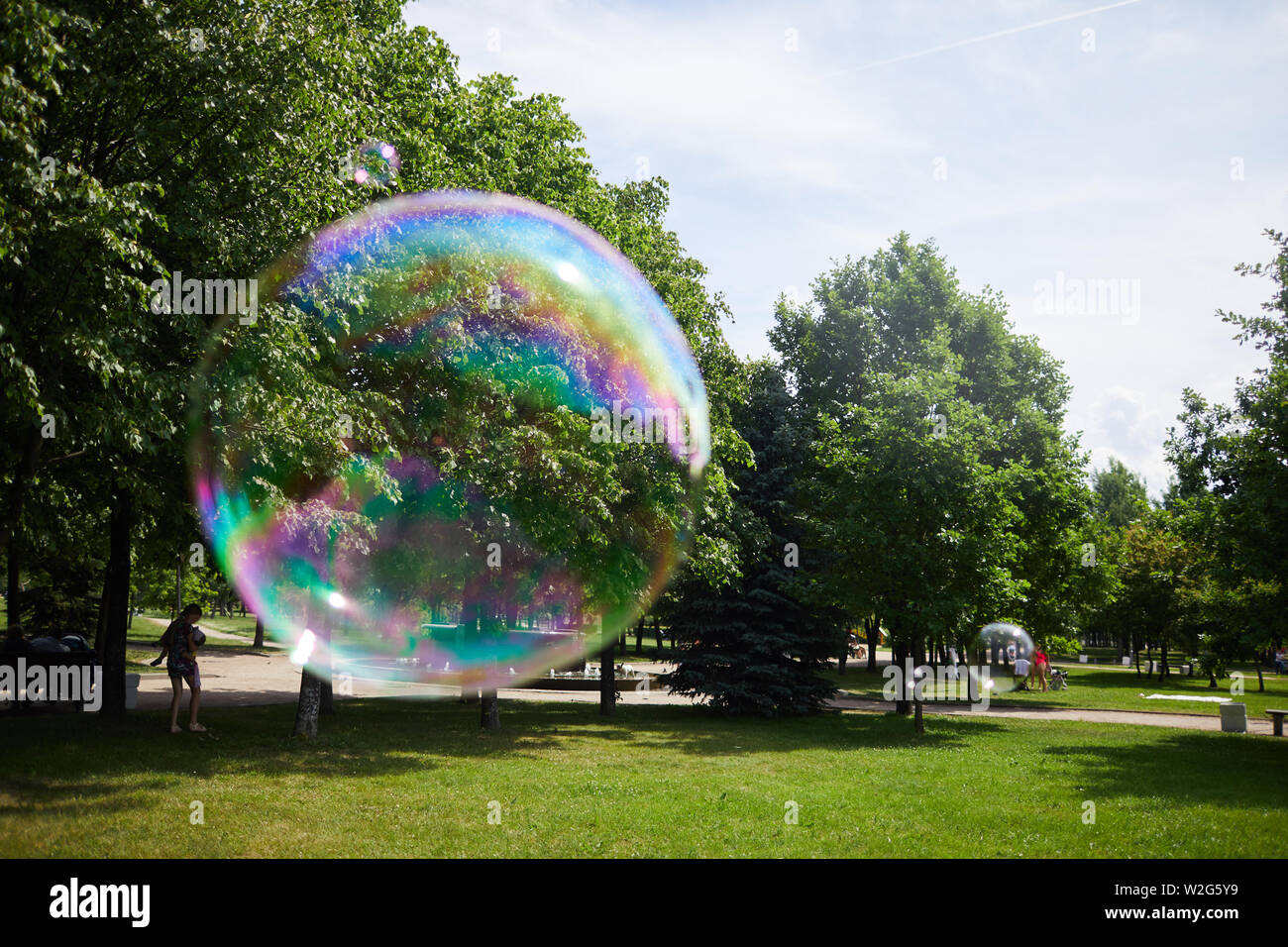 Big colorful soap bubble flying in summer park with green trees and ...