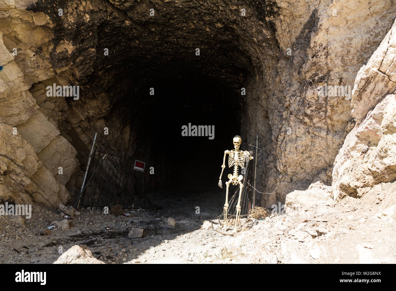Skeleton in the mouth of a mine by No Trespassing sign in the desert ...