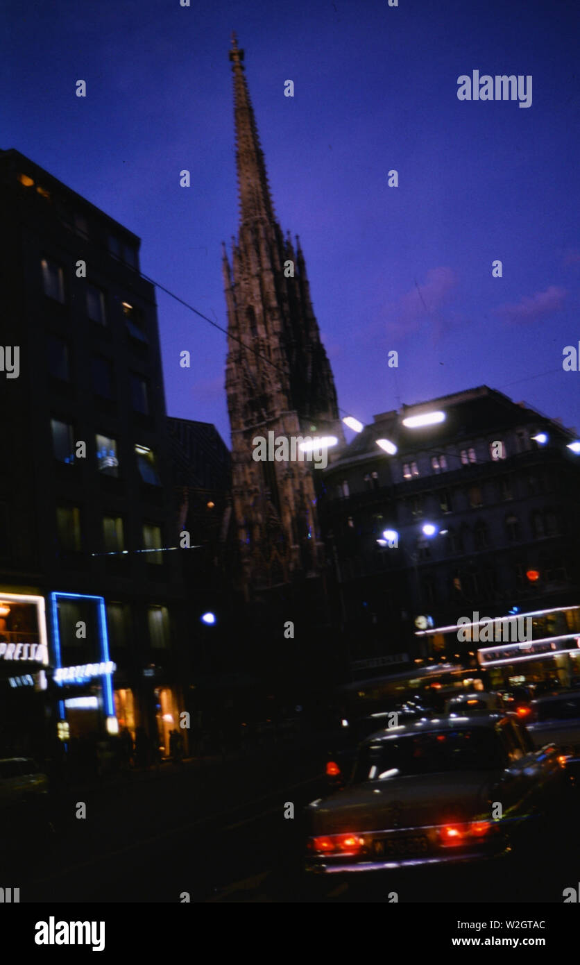 Artistic 1960s street scene at night with large church steeple rising ...