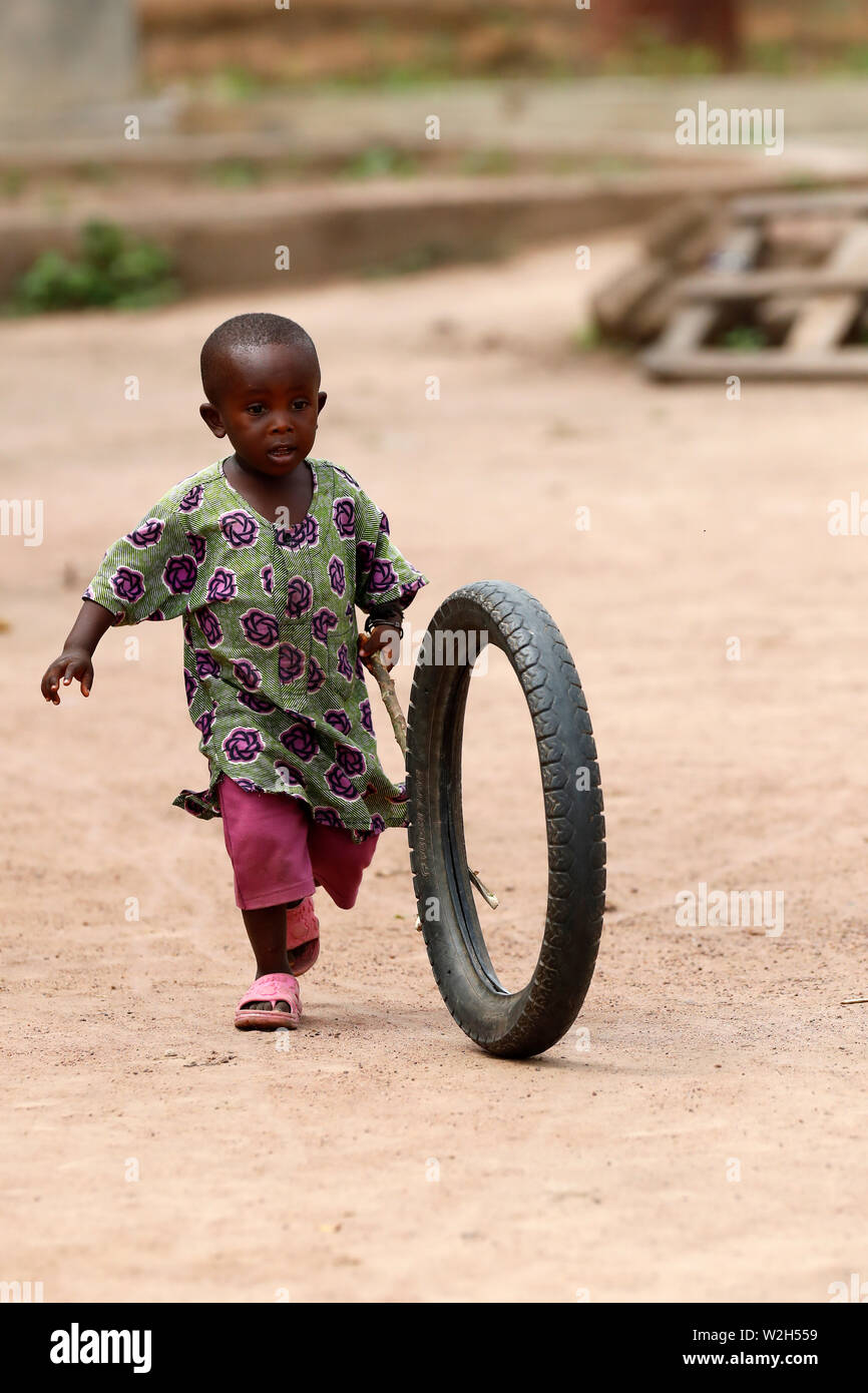 African boy playing with a motorcycle tyre and a stick as a toy. Datcha ...