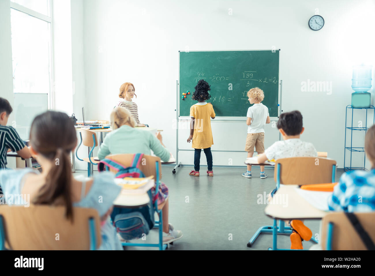 Teacher watching her class while two kids writing Stock Photo - Alamy