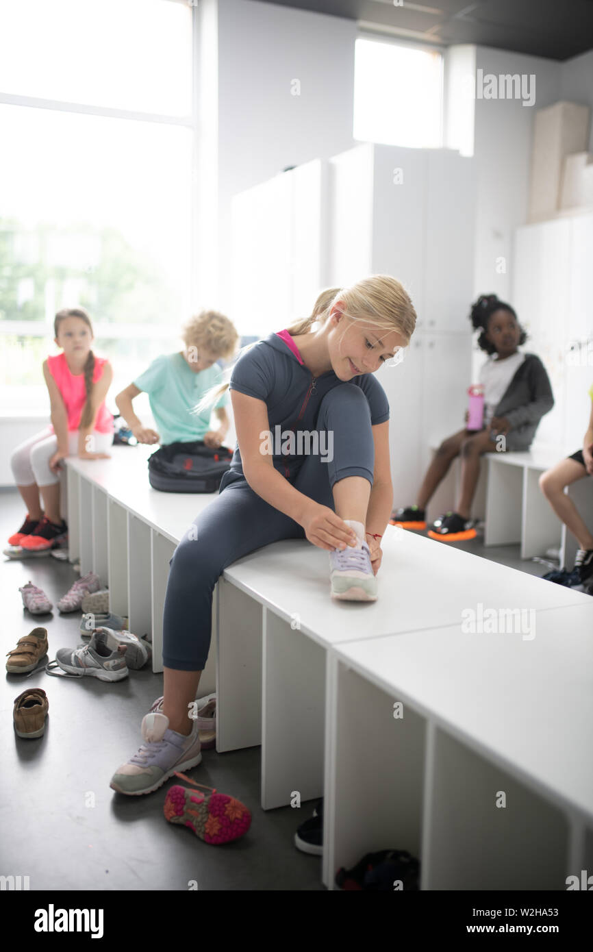 Smiling girl tying her shoes sitting on the bench Stock Photo - Alamy