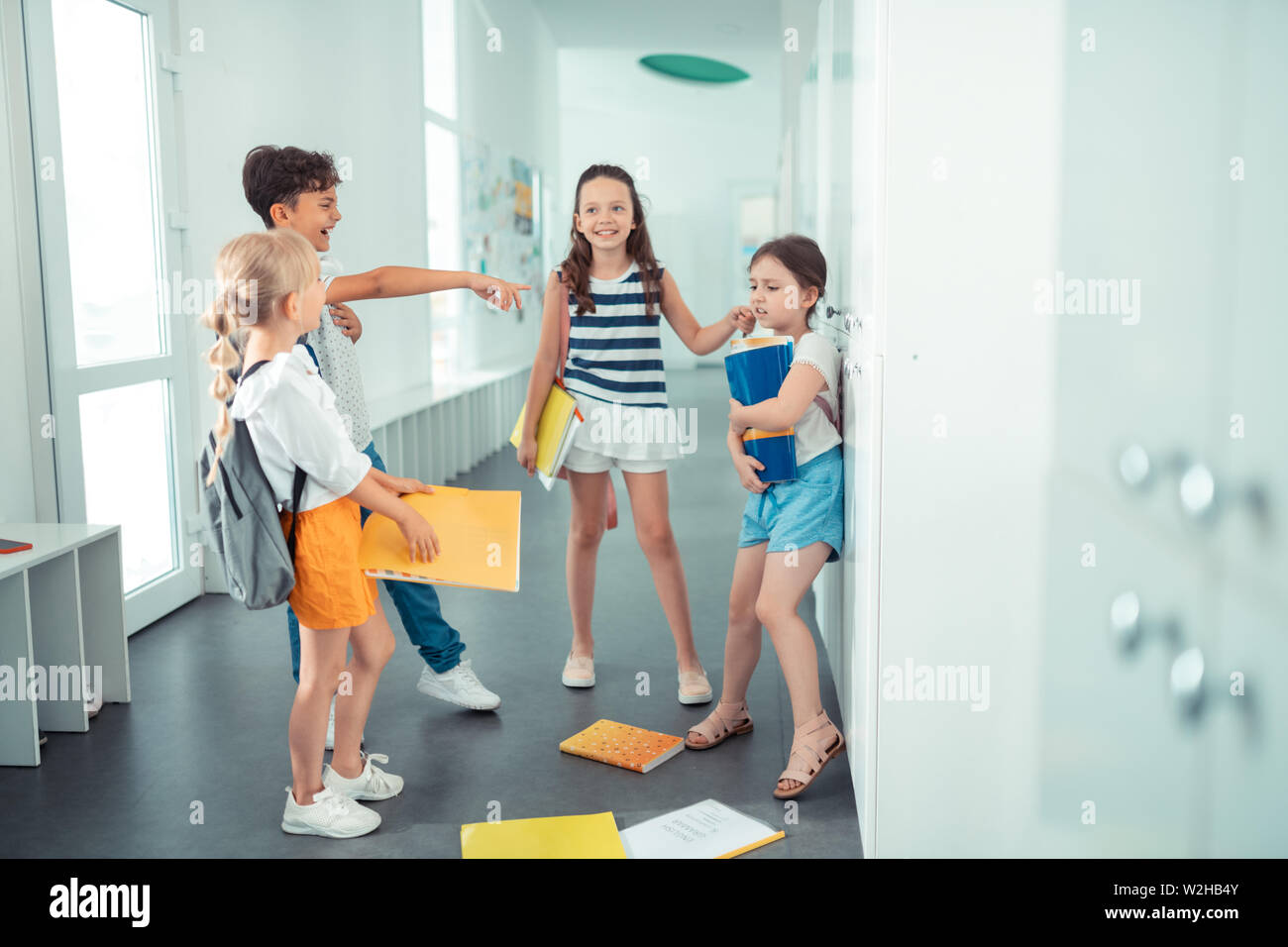 Rude children throwing papers of girl on the floor while bullying her ...