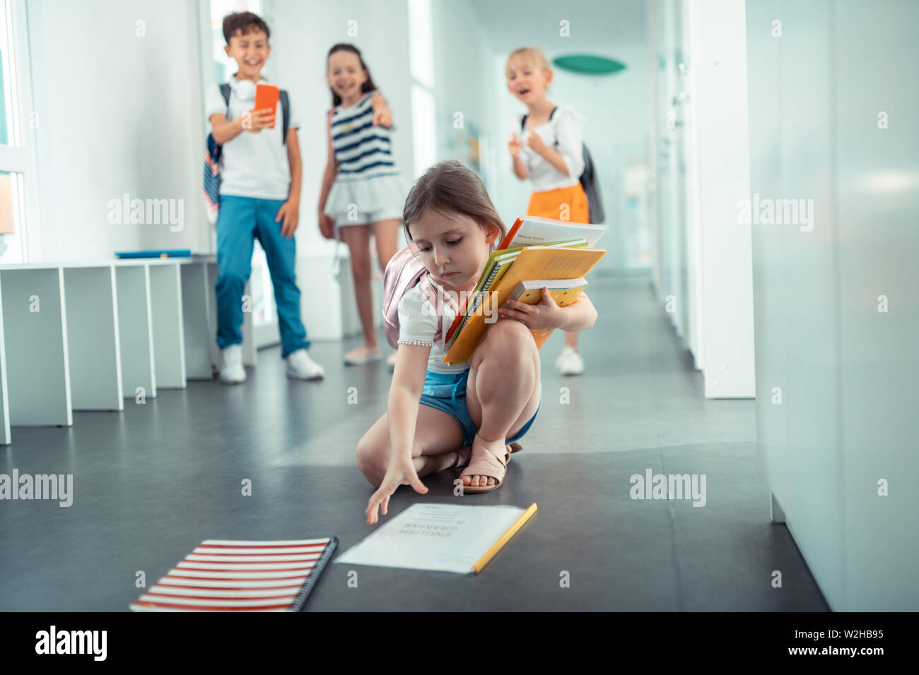 Girl picking up books from floor after boy pushed her Stock Photo - Alamy