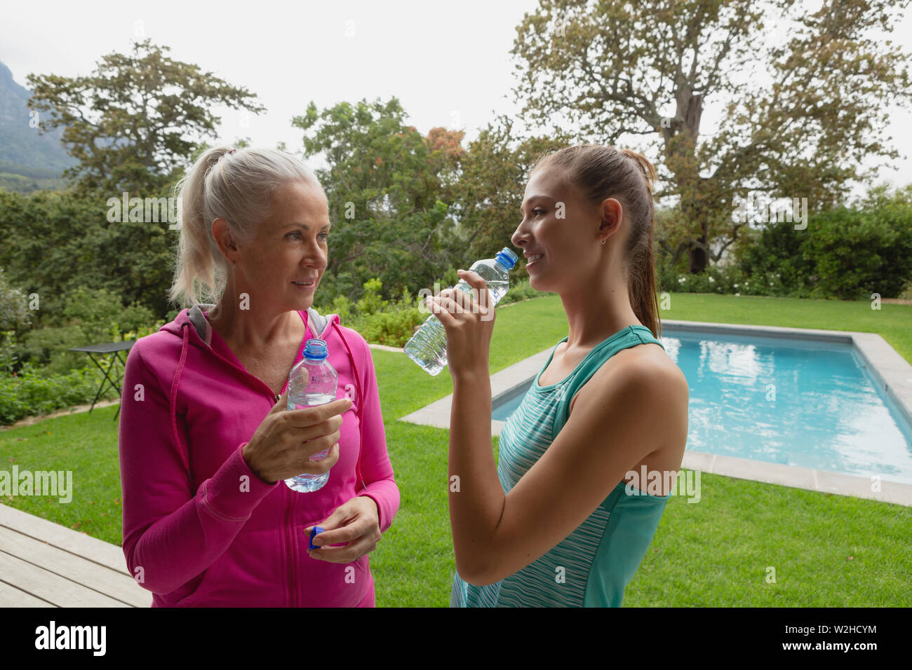 Female trainer and active senior woman drinking water in the backyard ...