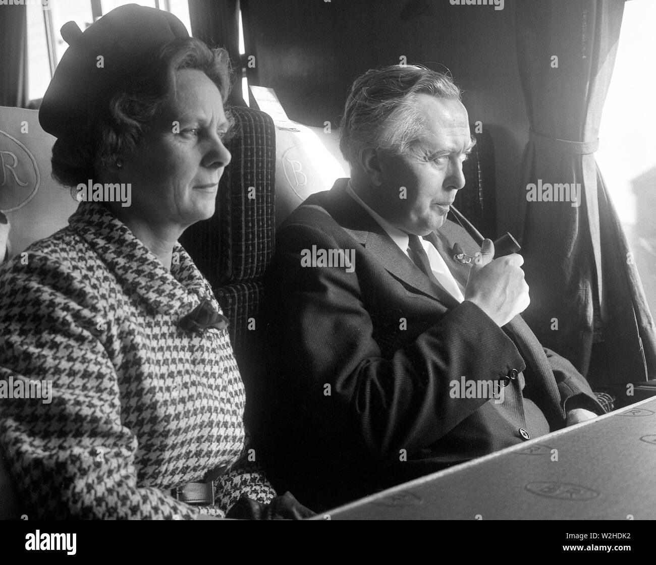 Harold Wilson thoughtfully draws at his pipe as, with his wife seated ...