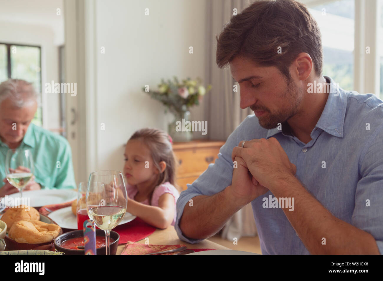 Multi-generation family praying before having food on dining table ...