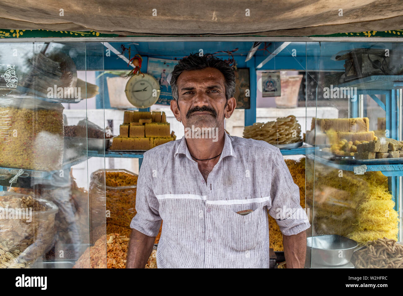 A portrait of a Indian man in front of his food and snacks cart in a ...