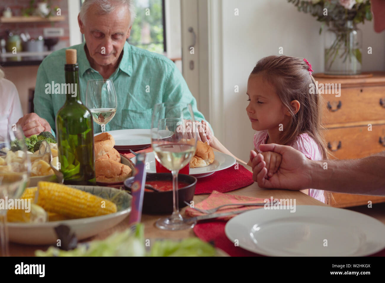 Multi-generation family praying before having food on dining table ...