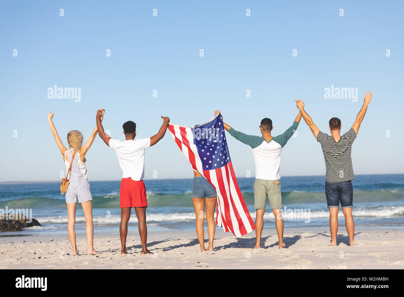 Group of friends standing together with American flag and raising hands ...