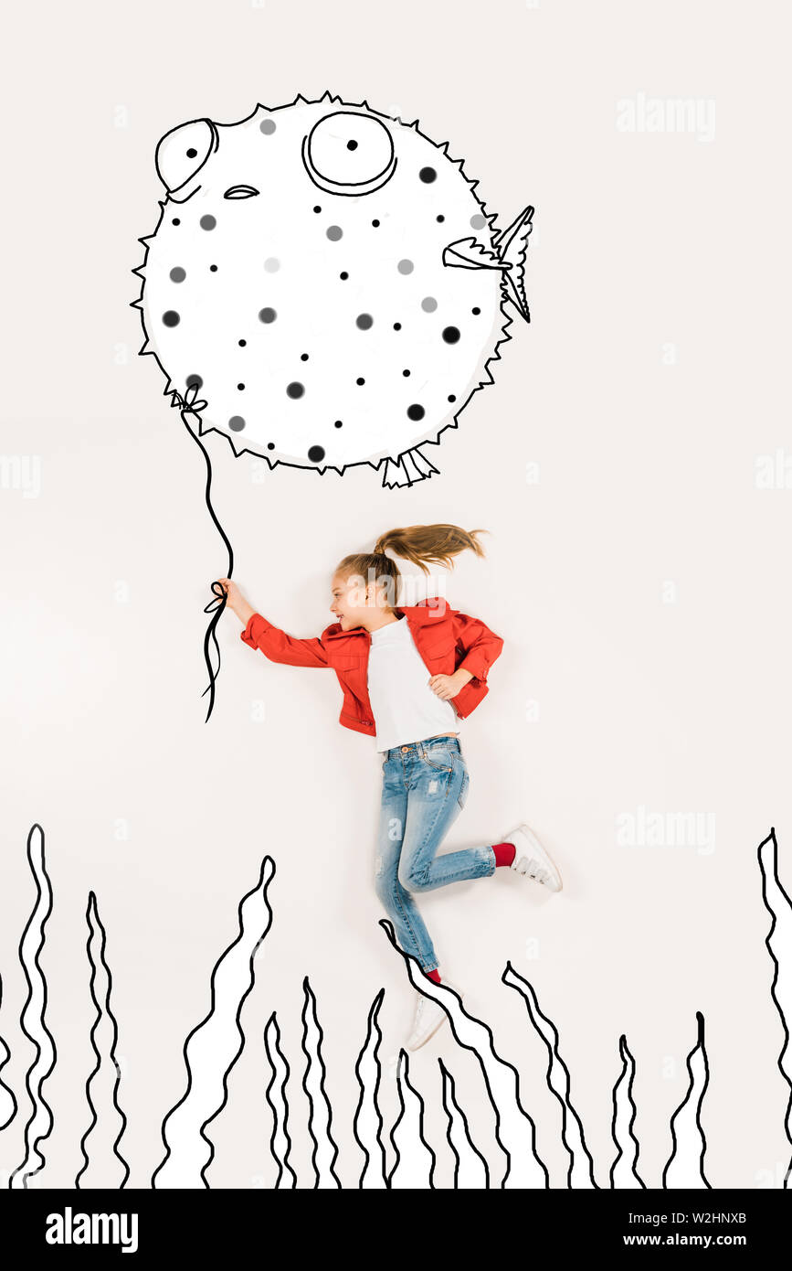 top view of cheerful child holding puffer fish and smiling on white ...