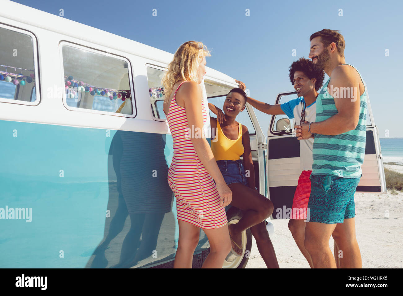 Group of friends talking with each other near camper van at beach in ...