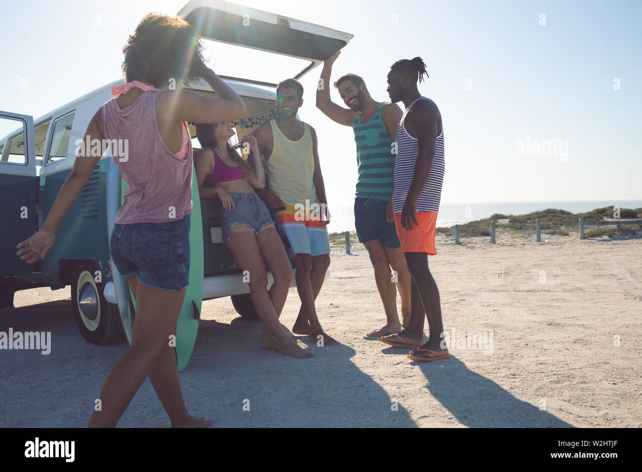 Group of friends interacting with each other near camper van at beach ...