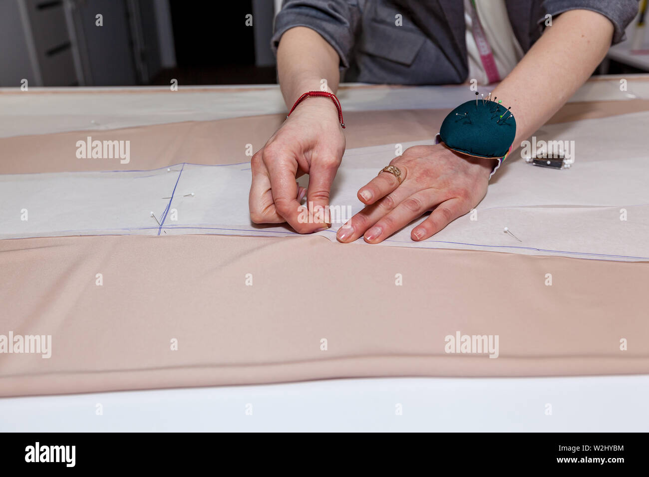 Female tailor hands with cloth, pattern and needle in the workshop ...