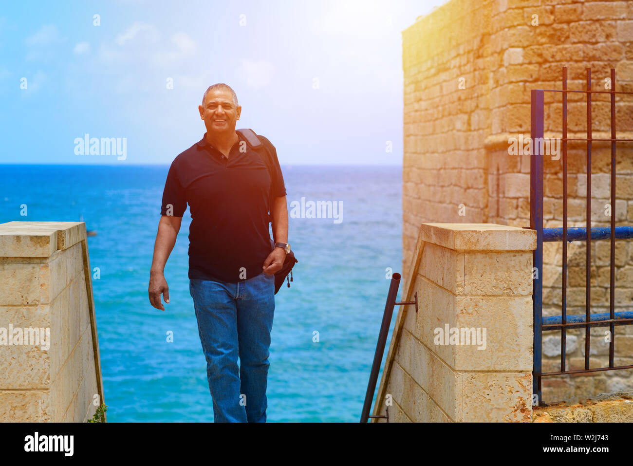 Smiling trendy tourist elderly man with black t-shirt walking by old ...