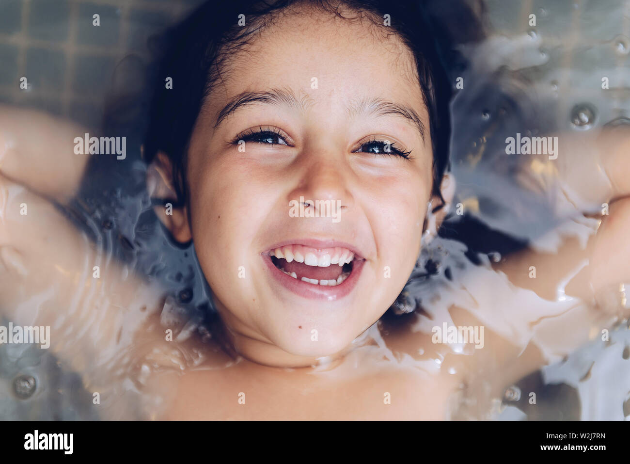 portrait of a happy pretty little girl laughing lying in the tub while ...
