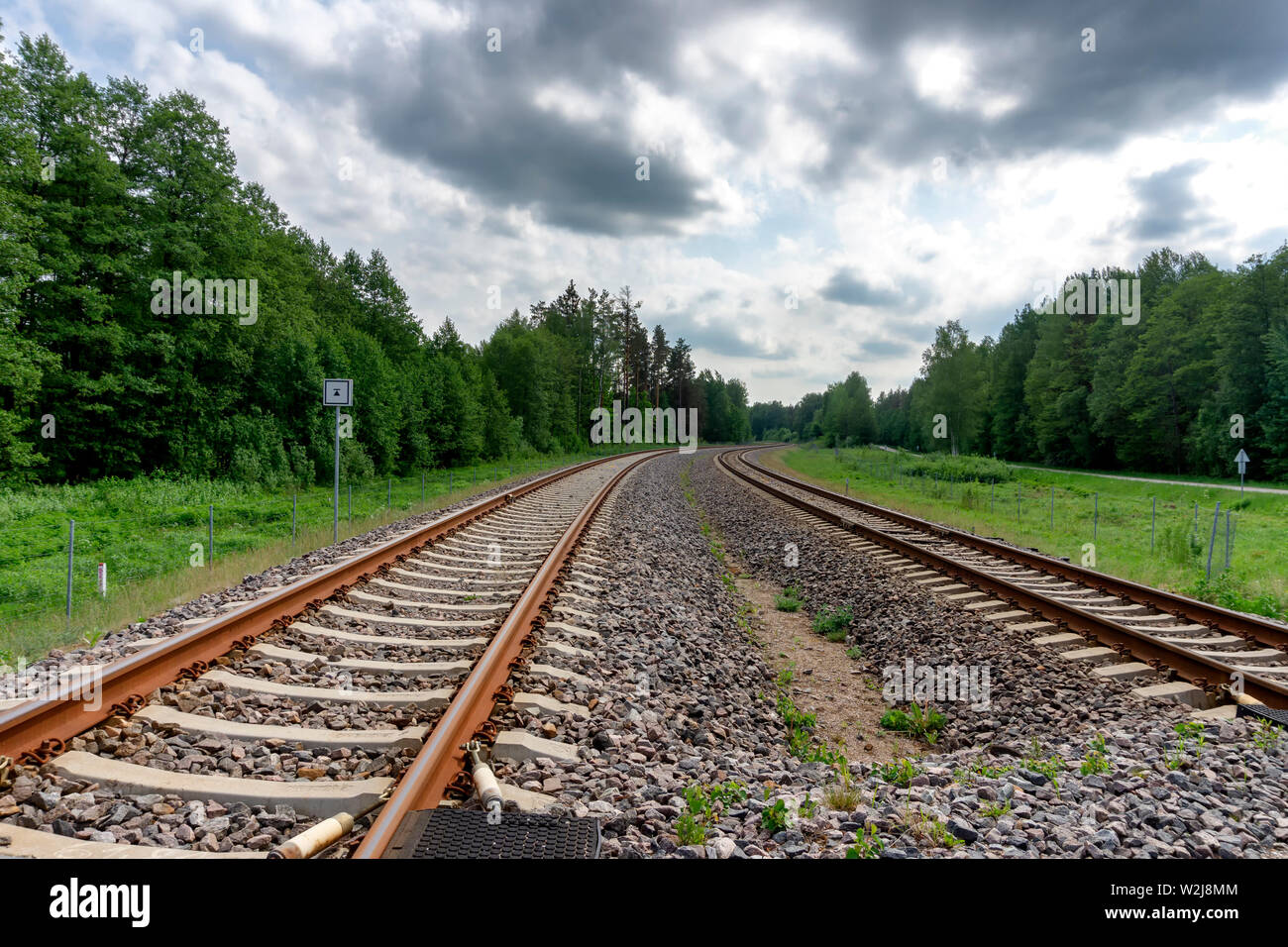 Curving railroad track through the forest against a blue sky and white ...