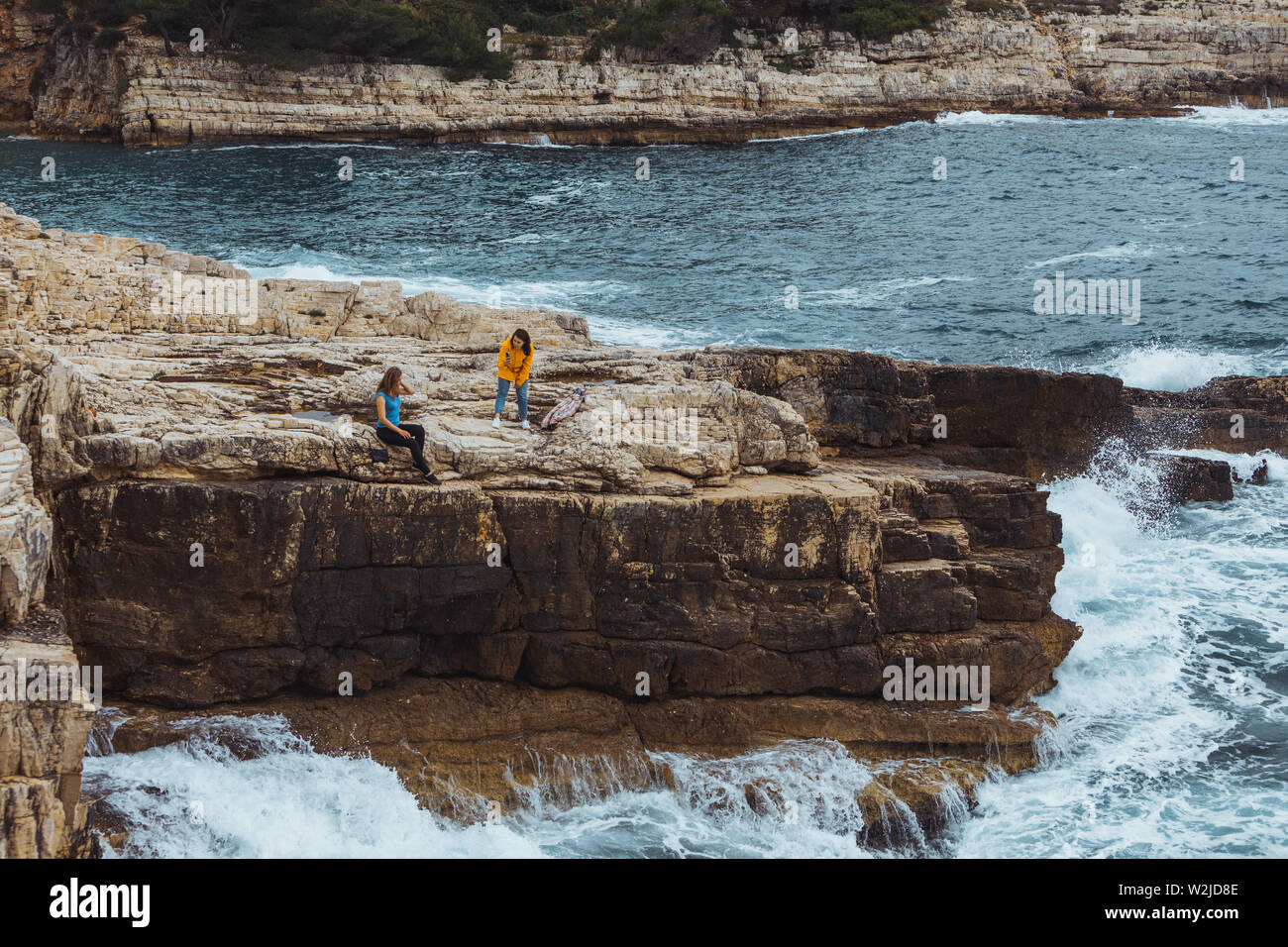 two young adult women at cliff looking at storm sea. overcast weather ...