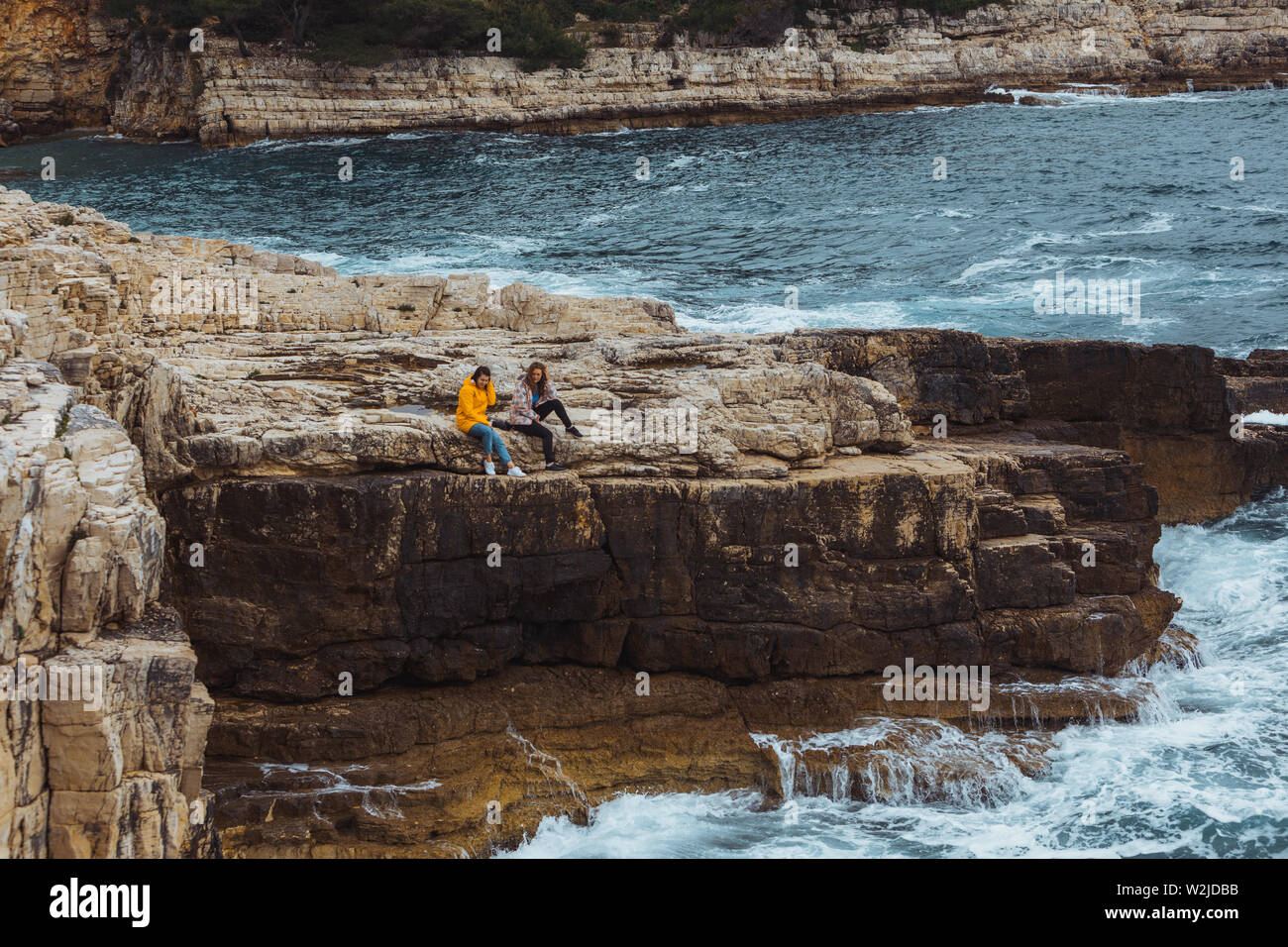 two young adult women at cliff looking at storm sea. overcast weather ...
