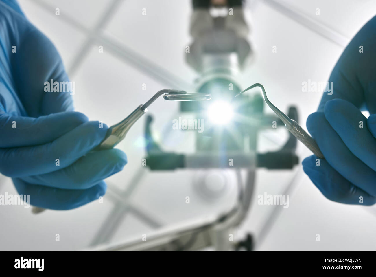 Doctor in blue latex gloves is looking into a dental microscope with a ...