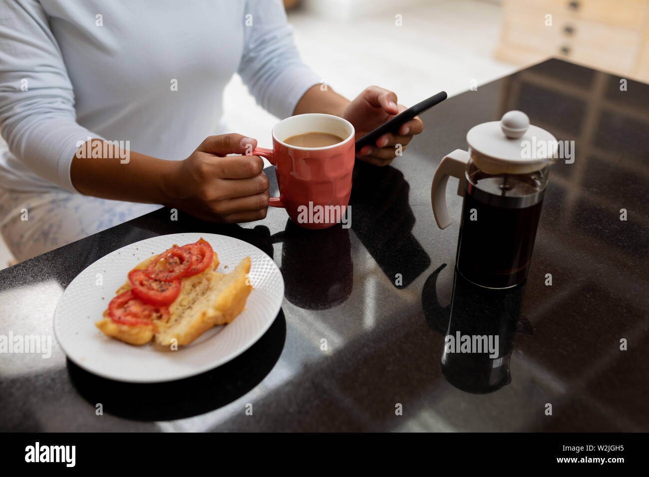 Woman using mobile phone on a dining table at kitchen Stock Photo - Alamy