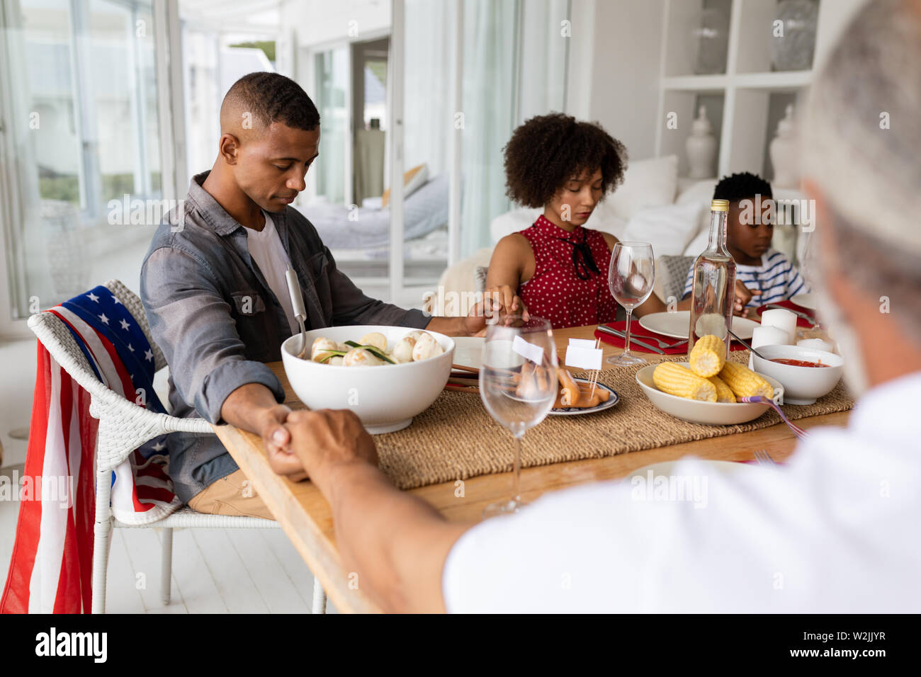Multi-generation family praying before having meal on dining table ...