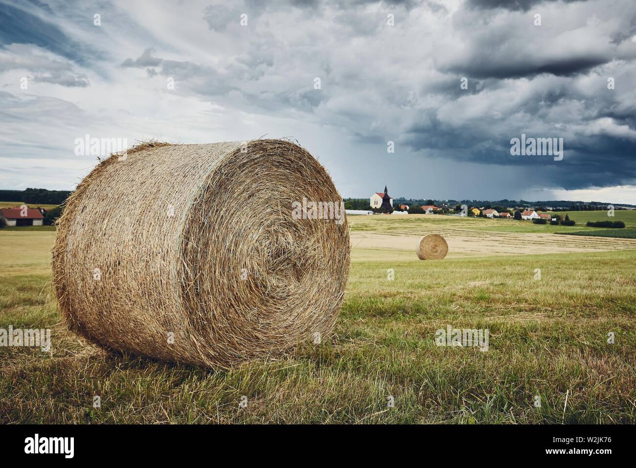 Straw bales stacked on field against landscape with village. Themes ...
