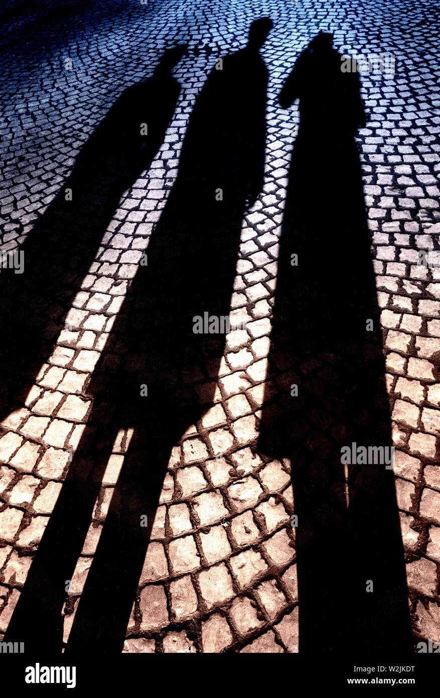 Three shadows of men wearing long coats on cobblestone street Stock ...
