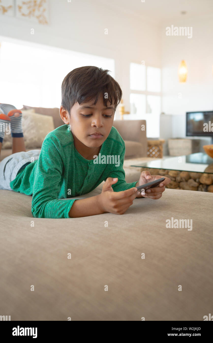 Boy playing game on mobile phone while lying on sofa at home Stock ...