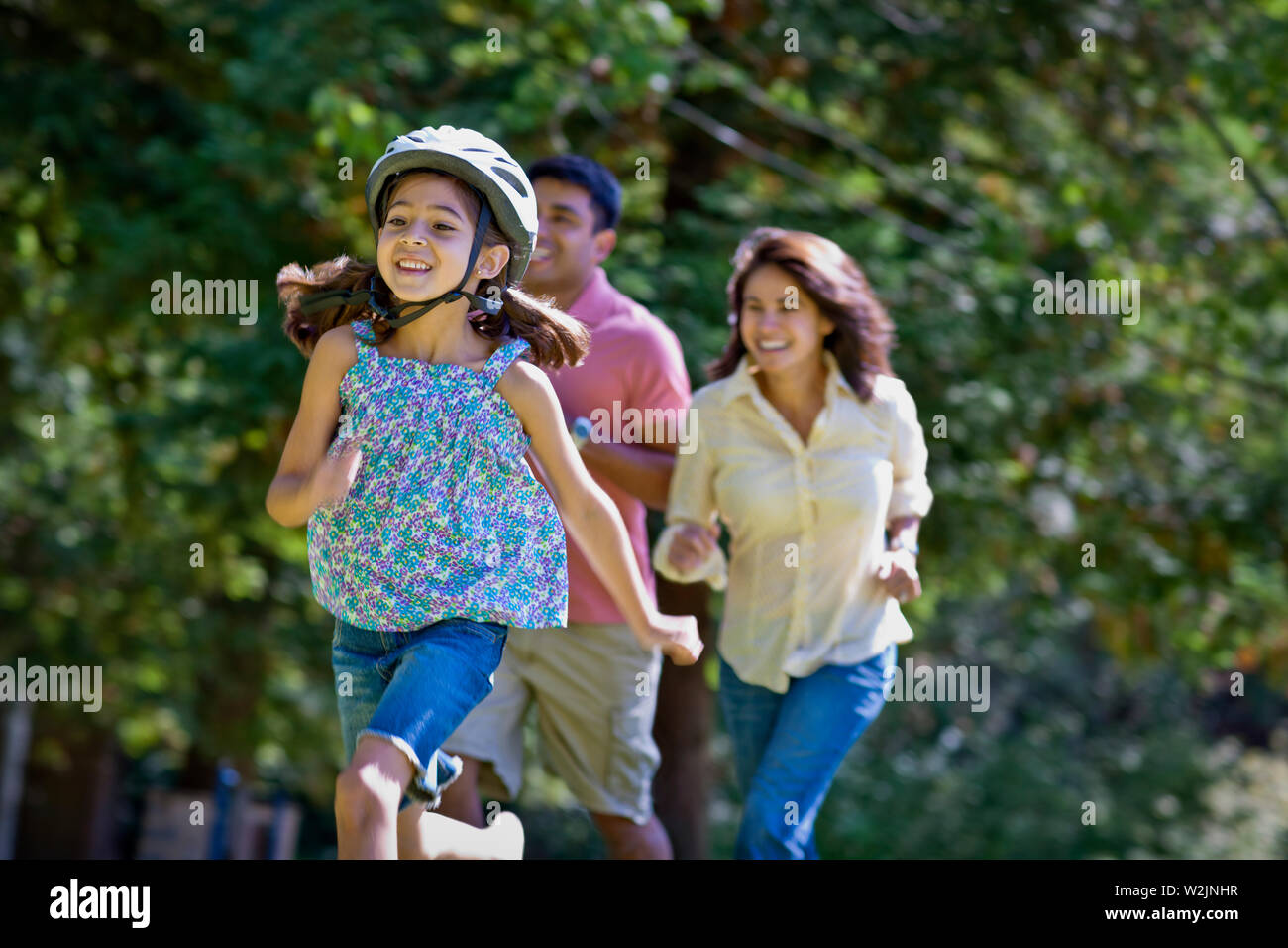 Parents chasing their playful young daughter through the park Stock ...