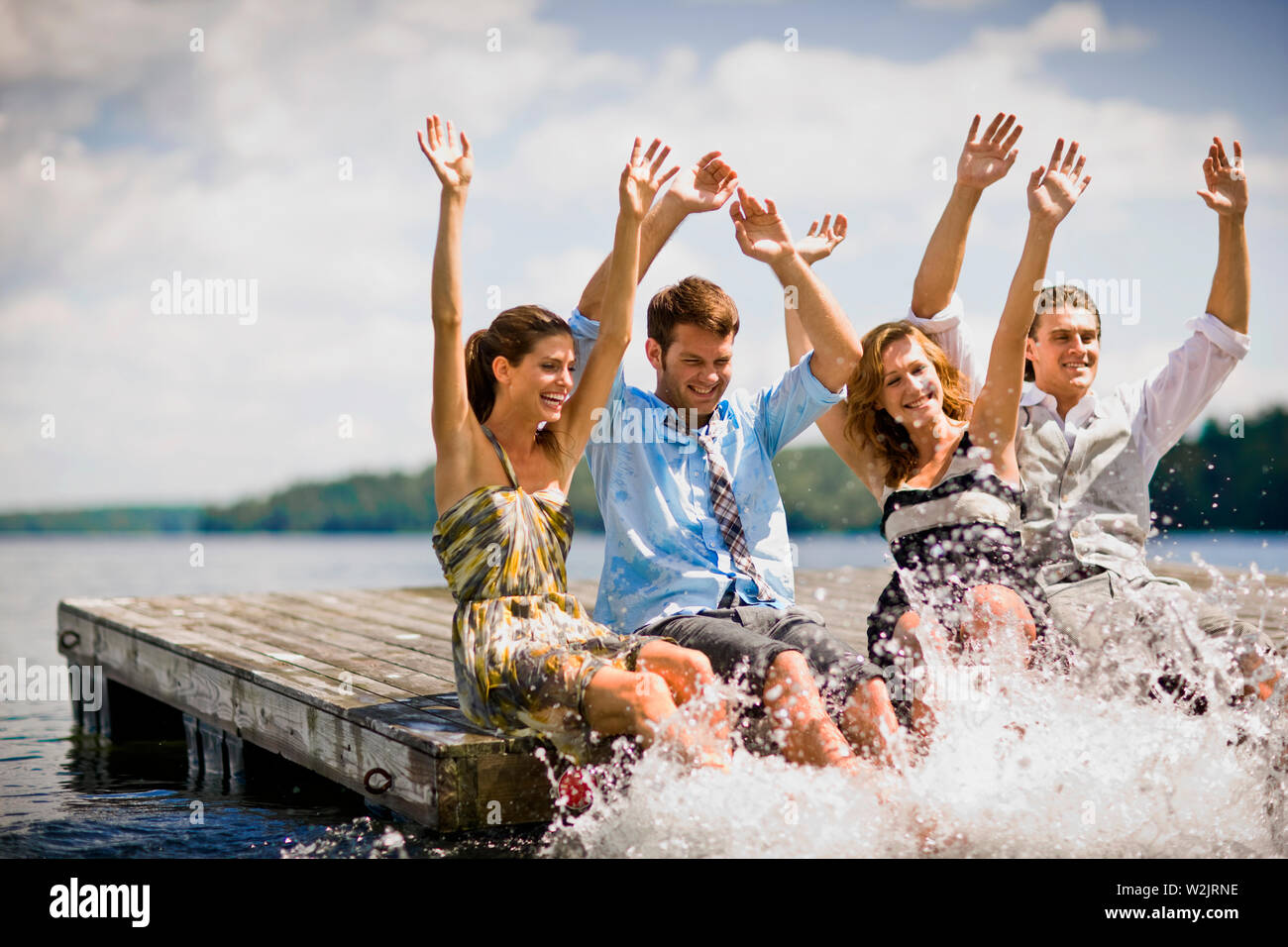 Group of friends sitting on a jetty, splashing in the lake with their ...